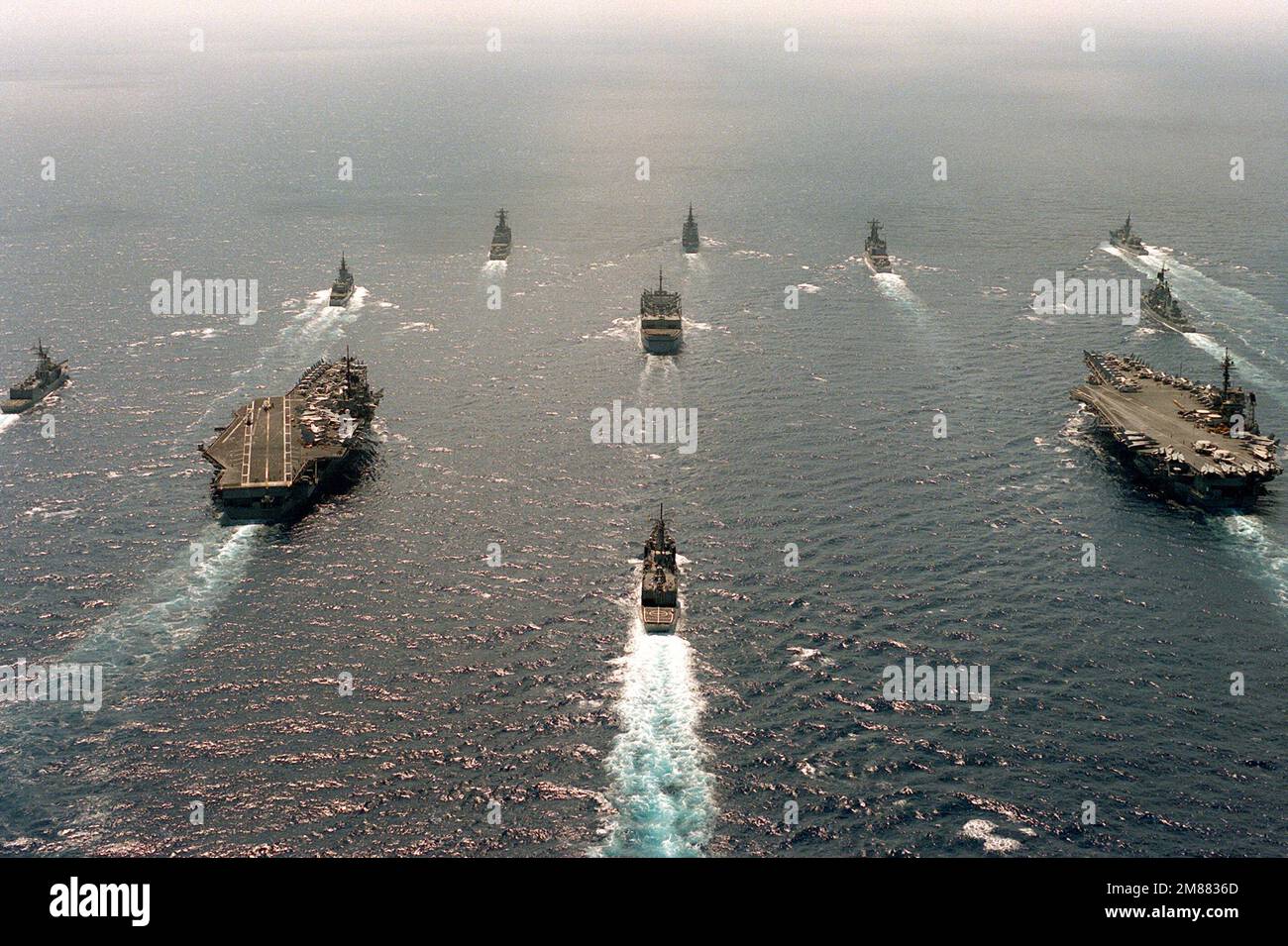 An aerial view of various ships underway in formation. They are ...