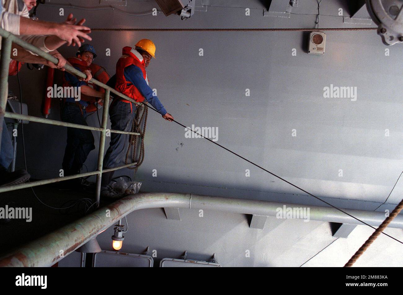 A crew member hauls a handling line inboard during an underway ...