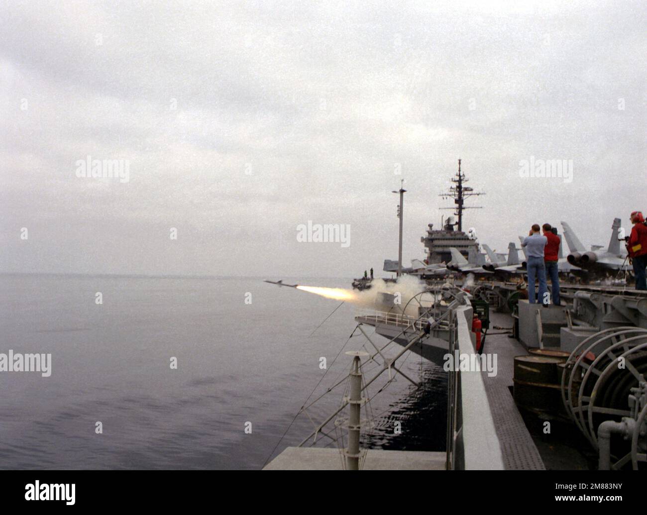 Flight deck crewmen standing near the ship's bow watch as a RIM-7 Sea ...