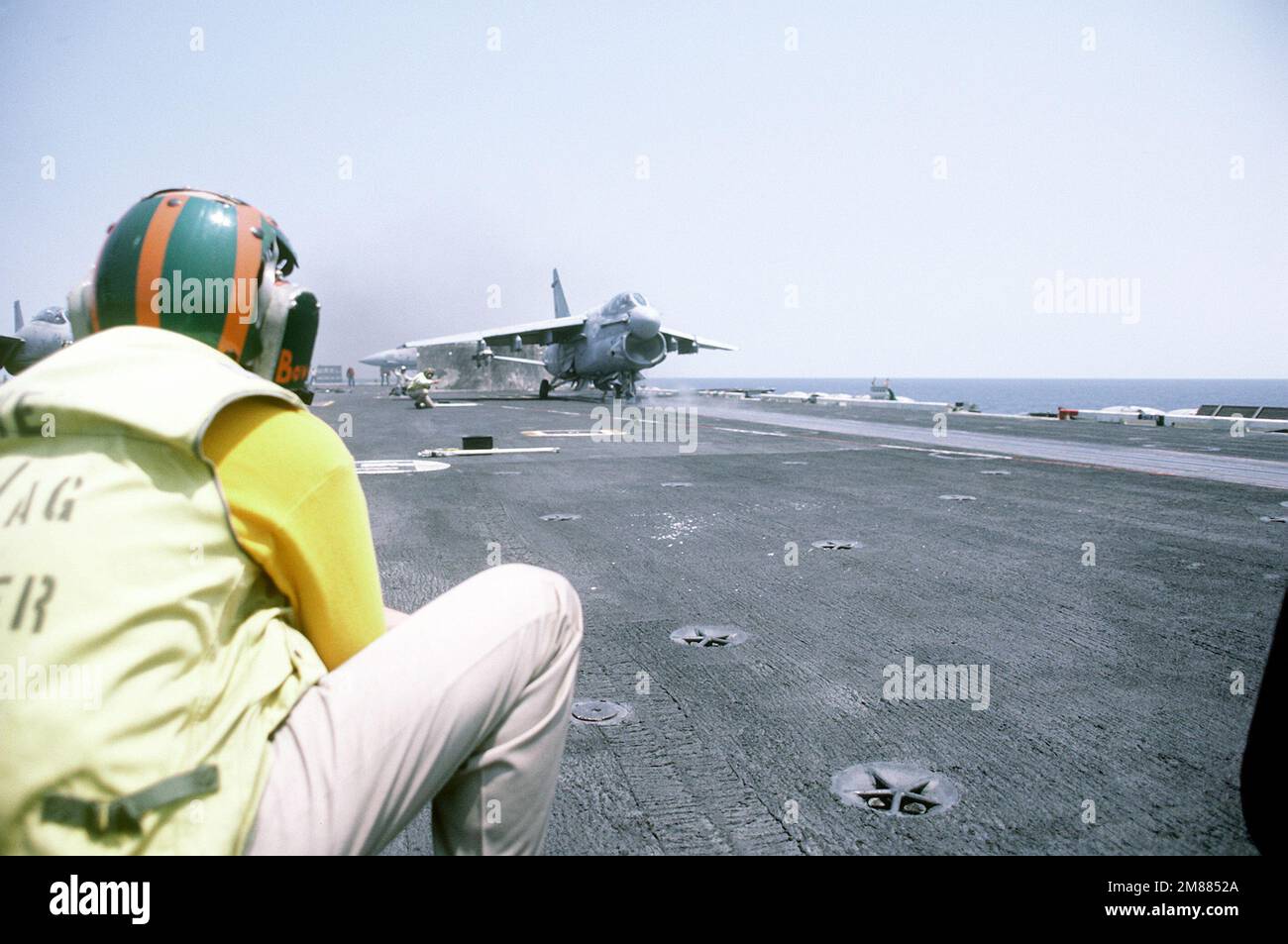 Flight deck crewmen stand by as an A-7E Corsair II aircraft is prepared ...