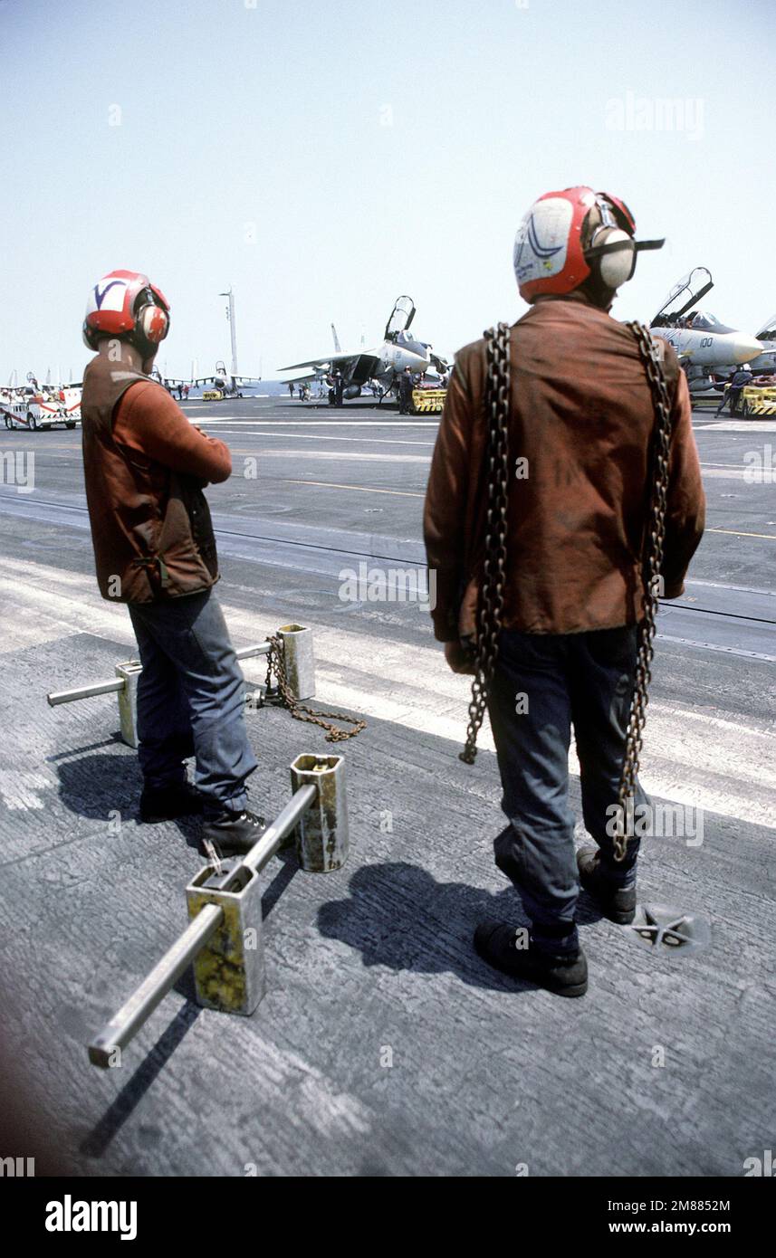 Flight deck crewmen stand by with chocks and tie-down chains during ...