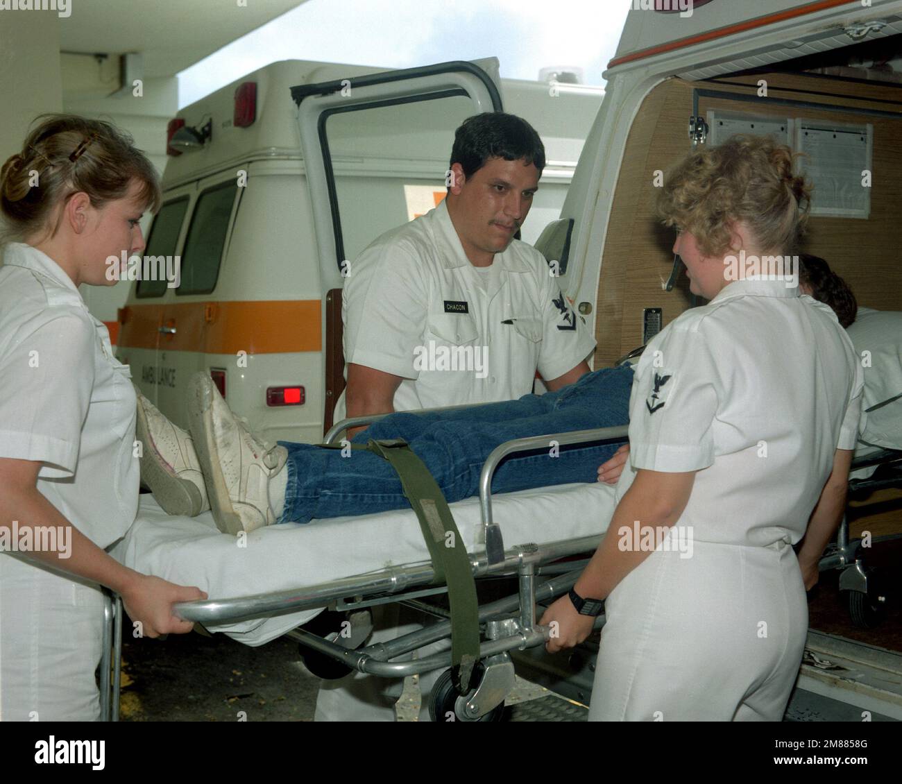 Three hospital corpsmen remove a patient on a gurney from an ambulance ...