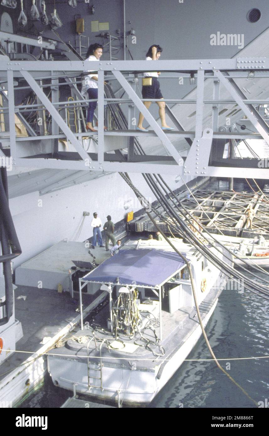Yard workers stand by in small craft tied up alongside the aircraft ...