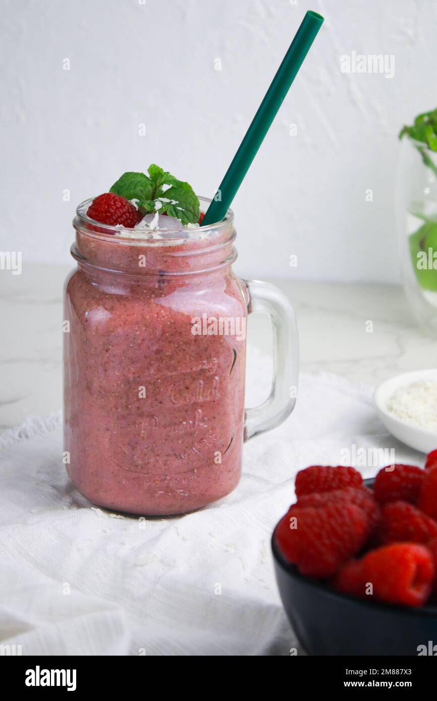 raspberry coconut smoothie with ice in a jar with straw, white ...