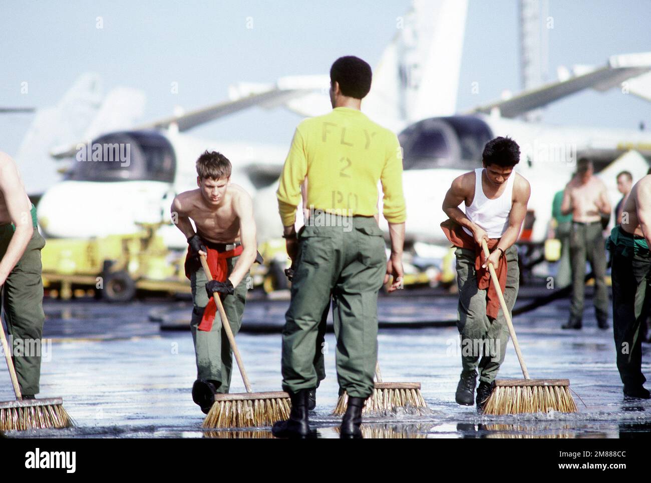 A petty officer supervises crew members as they scrub the flight deck ...