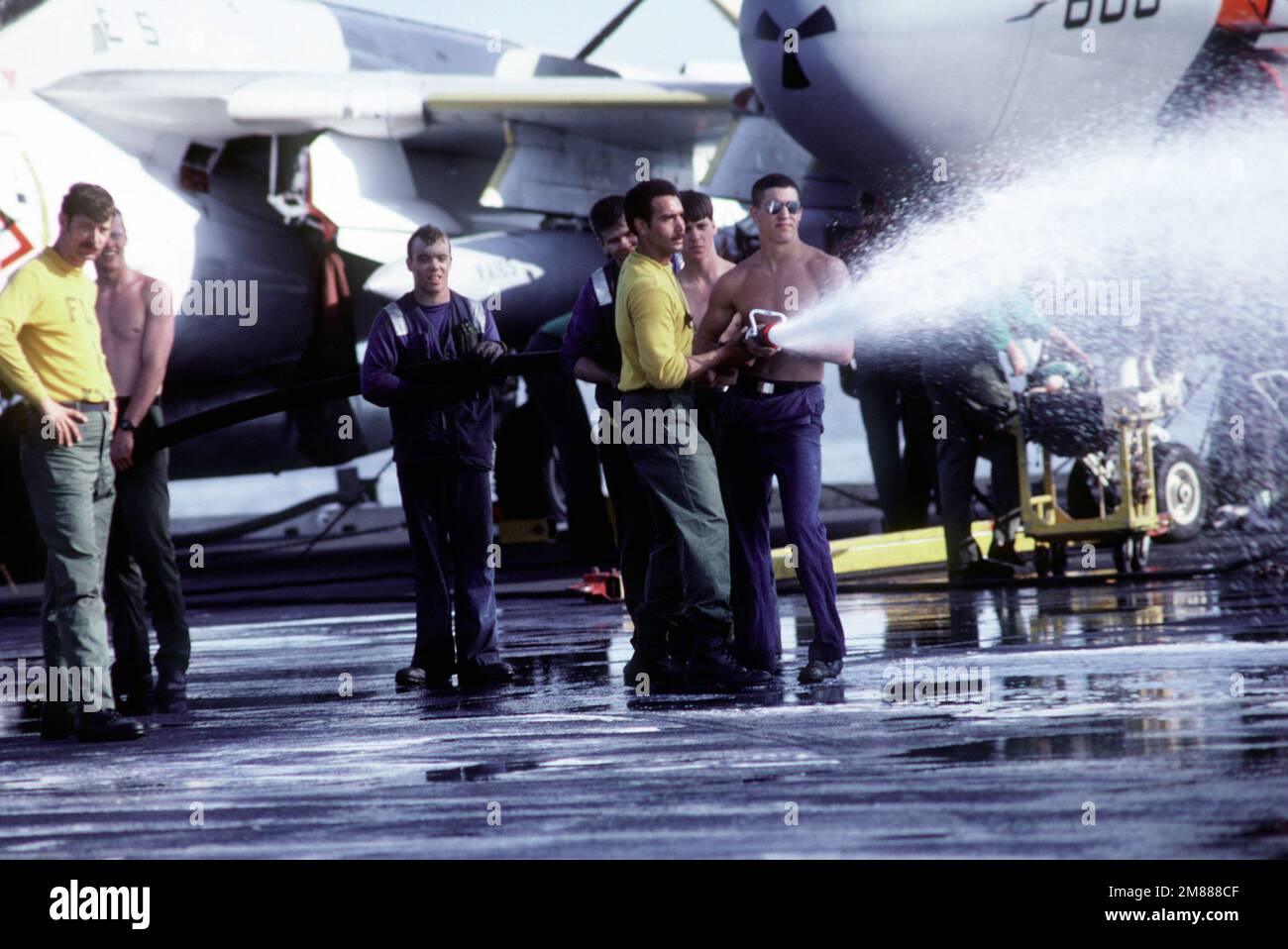 A petty officer assists crew members in hosing off the aircraft carrier ...