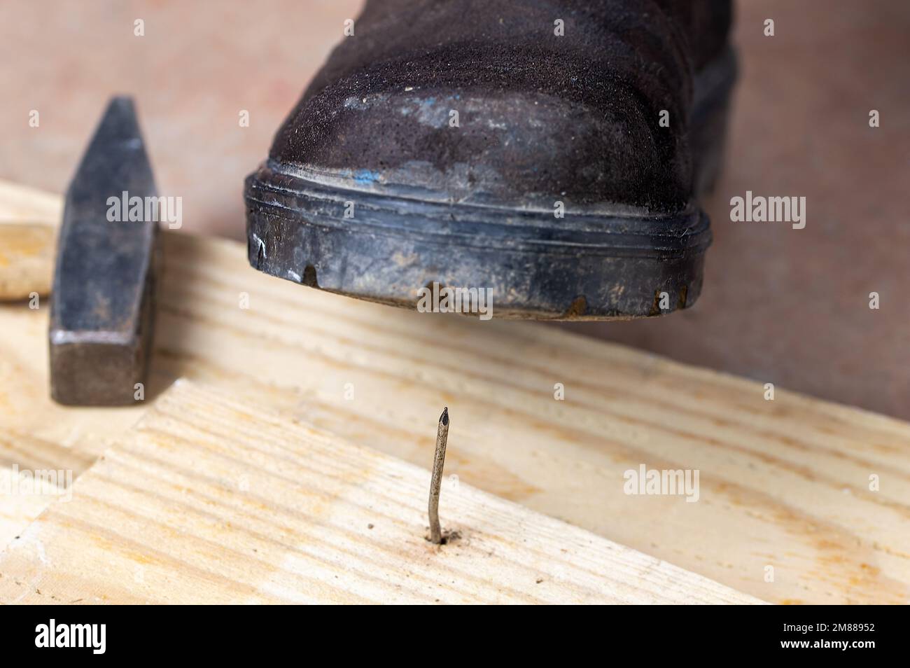 Close-up of man's foot stepping over there nail inserted in wooden ...
