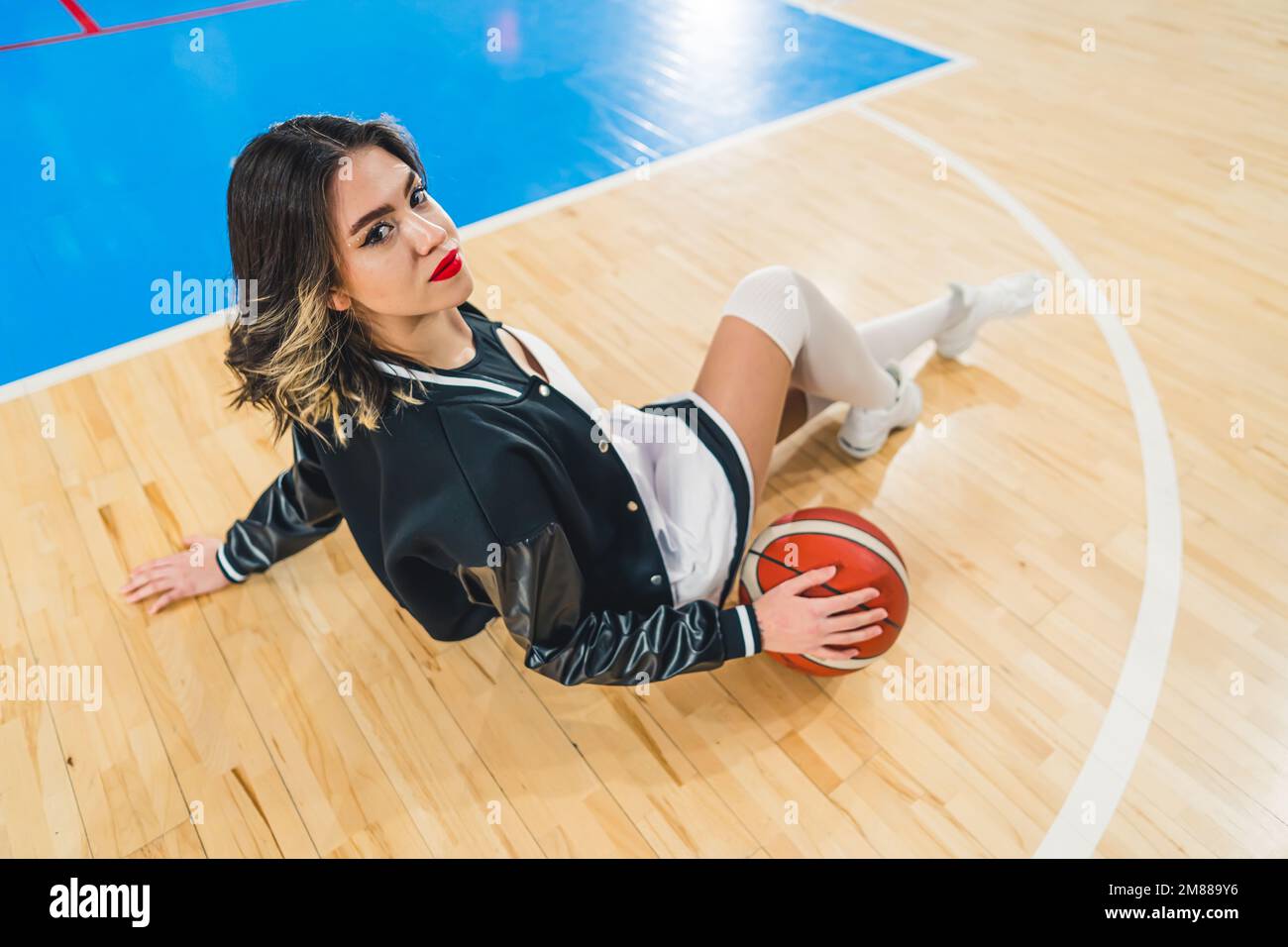Attractive cheerleader in mini-skirt sitting on the courts floor with ...