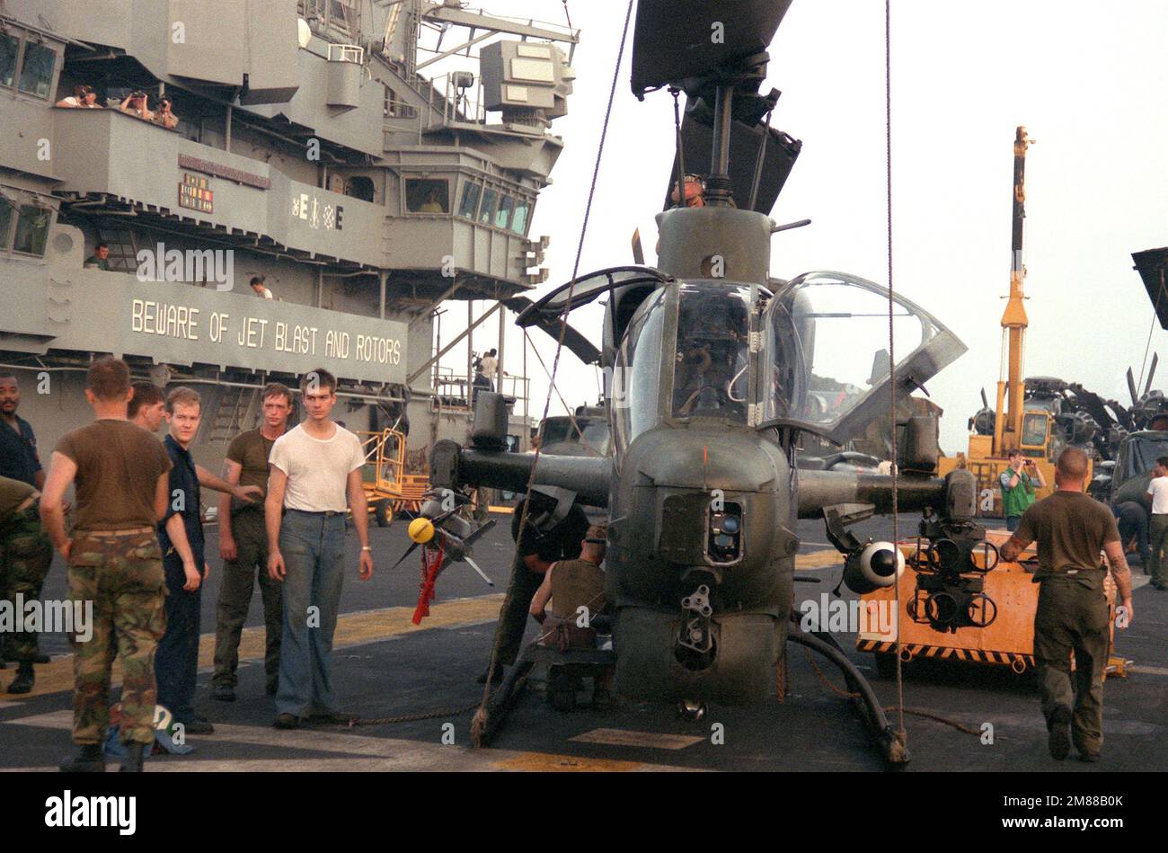 Crewmen service an AH-1 Sea Cobra helicopter on the flight deck of the ...
