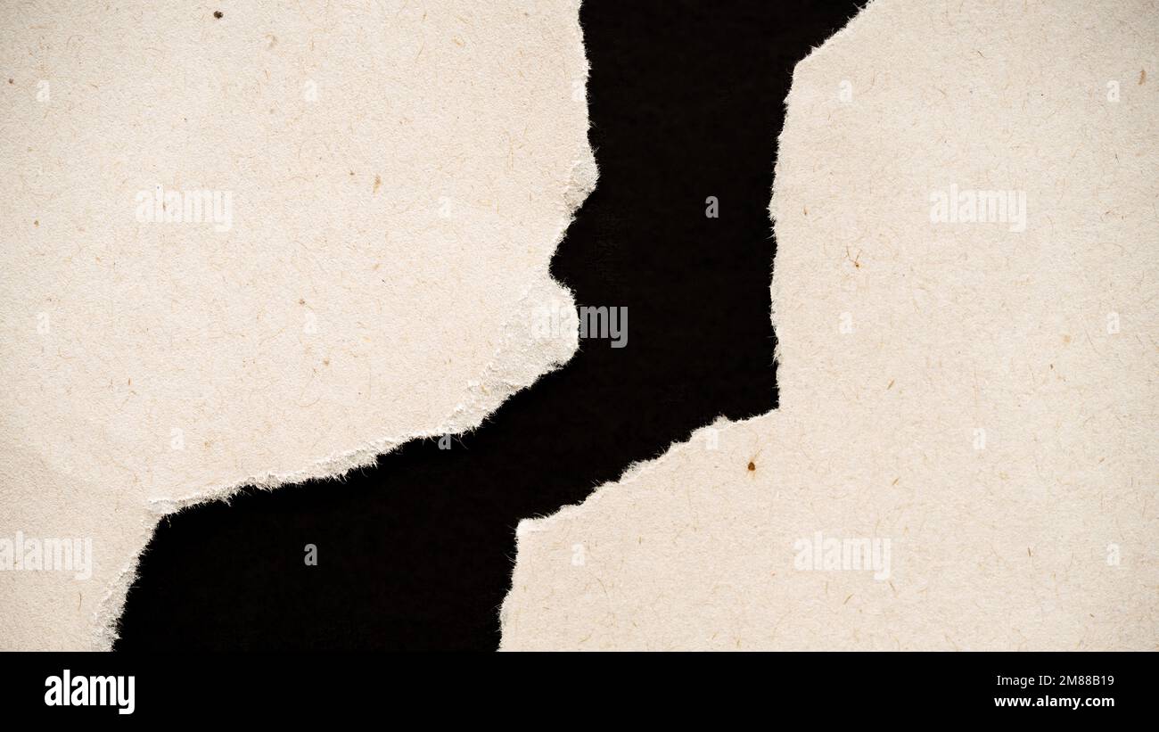 A macro shot of a torn paper with rough edges, on a black background ...