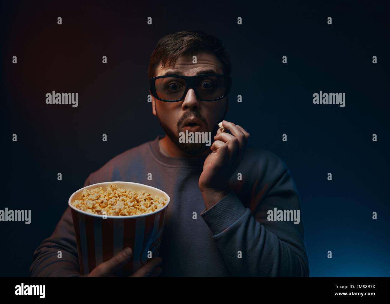A man eats popcorn and is horrified by a horror movie Stock Photo - Alamy