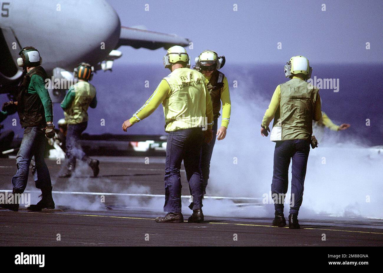 A plane director and flight deck crew members stand by as steam rises ...