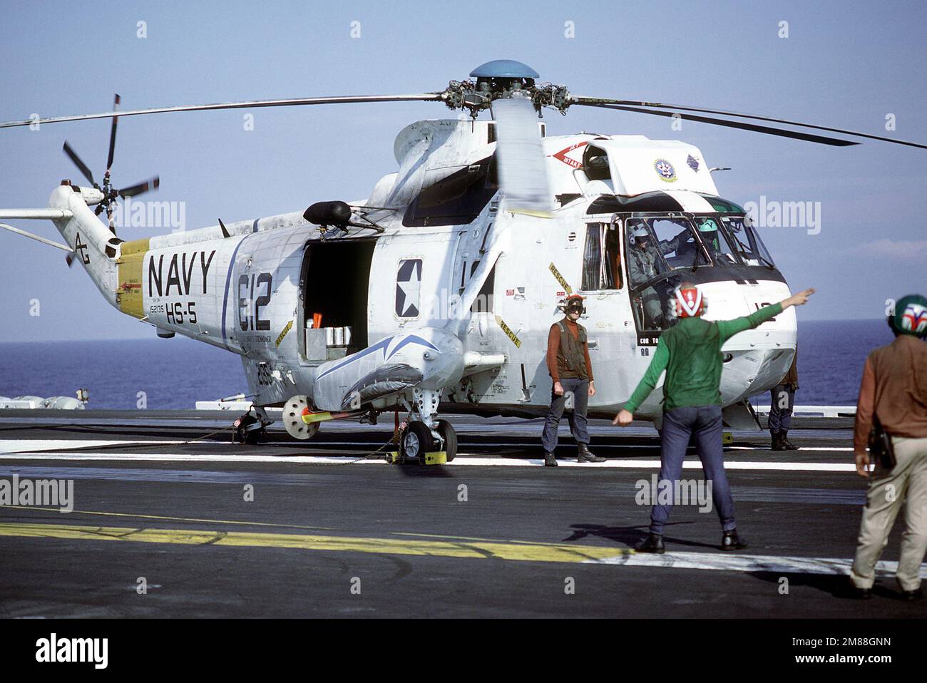A plane captain stands by as a flight deck crewman signals to the pilot ...