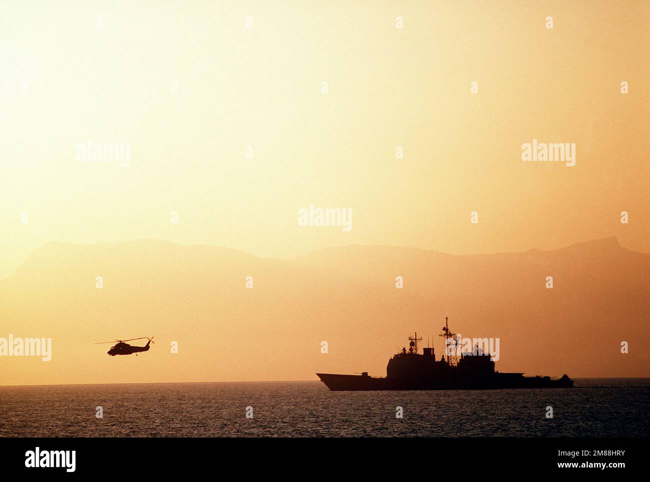 A silhouetted port view of the guided missile cruiser USS BUNKER HILL ...