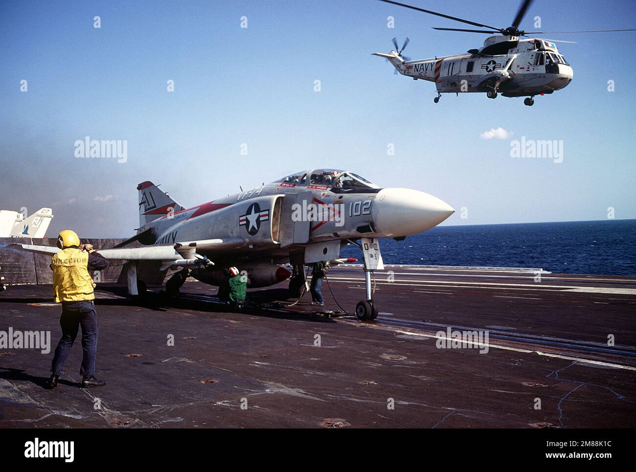 A plane director stands by as other flight deck crewmen prepare a ...