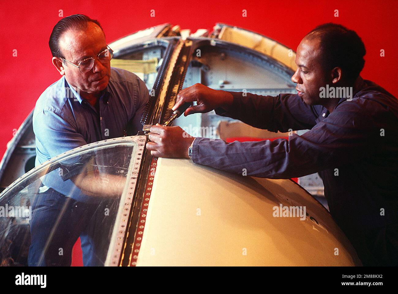 Two workers install a section of canopy on an F-111 aircraft cockpit ...