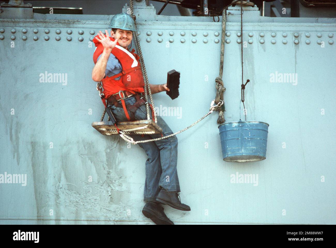 A sailor is suspended in a boatswain's chair while scrubbing the side ...