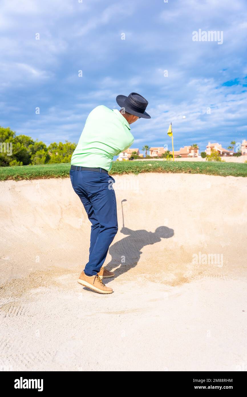 Man playing golf, getting the ball out of the bunker by hitting the ...