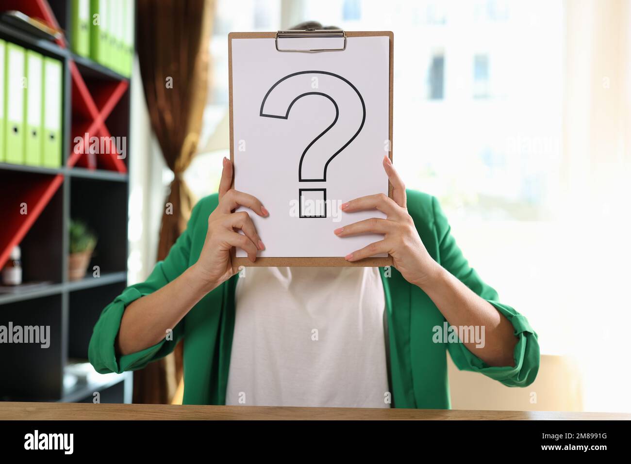 Business woman holding question mark in front of her face in office ...