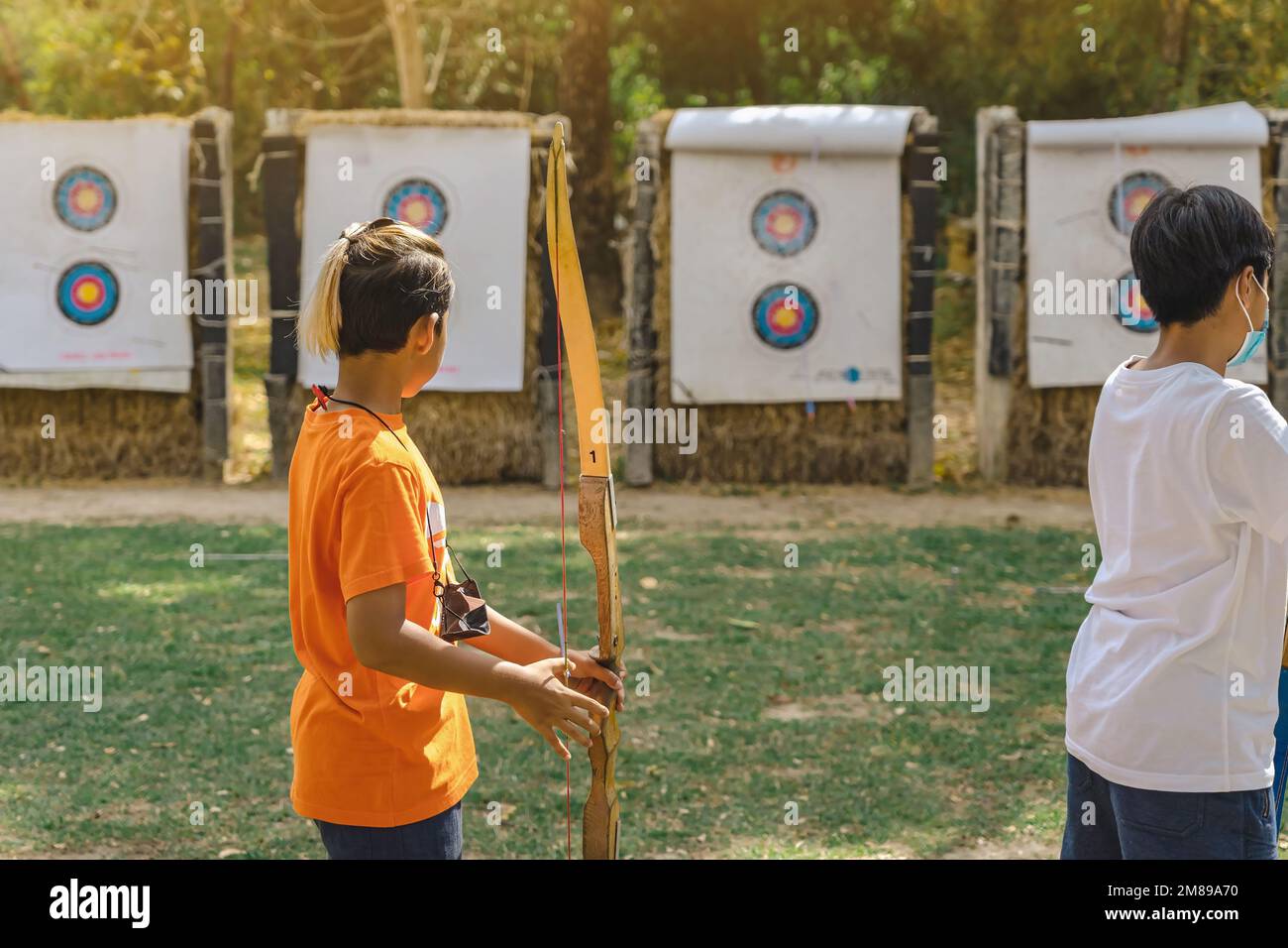 Back view of Asian boy wear face mask aims archery bow and arrow to ...