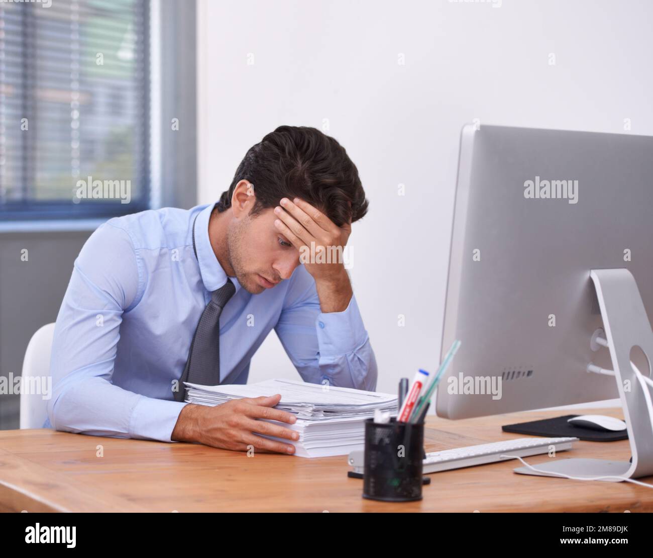 More paperwork. a young businessman looking frustrated while sitting at ...
