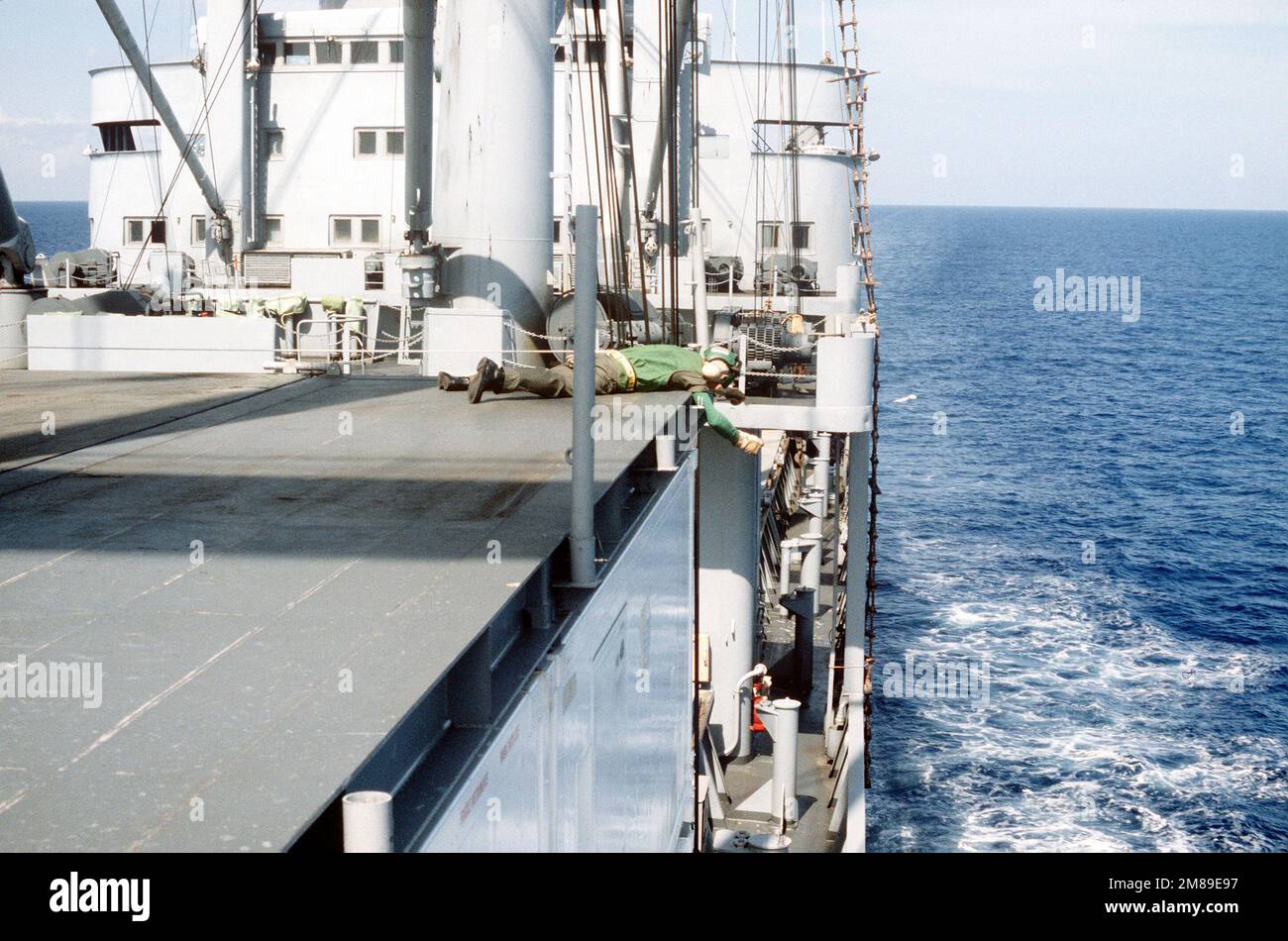 A crewman leans over the edge of the flight deck aboard the aviation ...