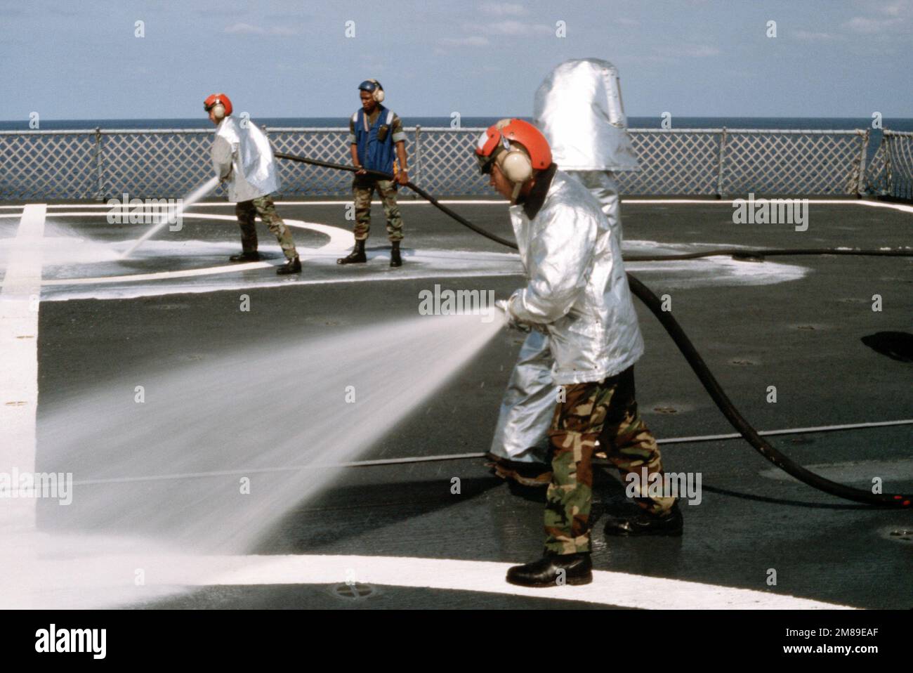 Marines in proximity suits hose down the flight deck of the aviation ...