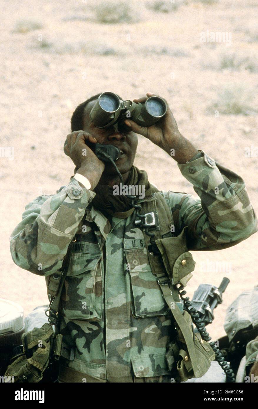 A soldier using binoculars reports his observations by field radio ...