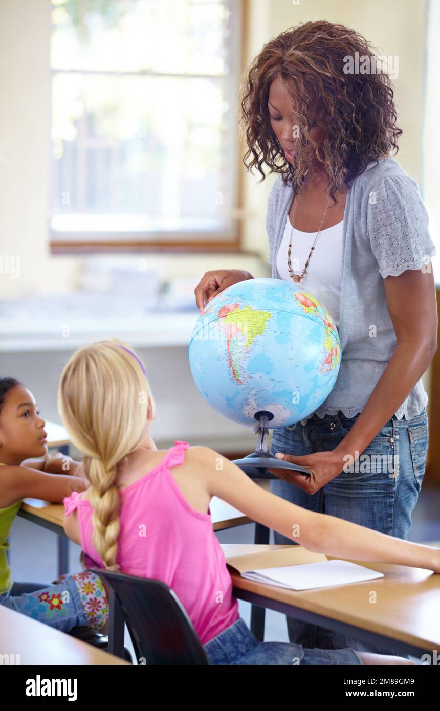 Teaching them about the world. A young teacher showing her class a ...
