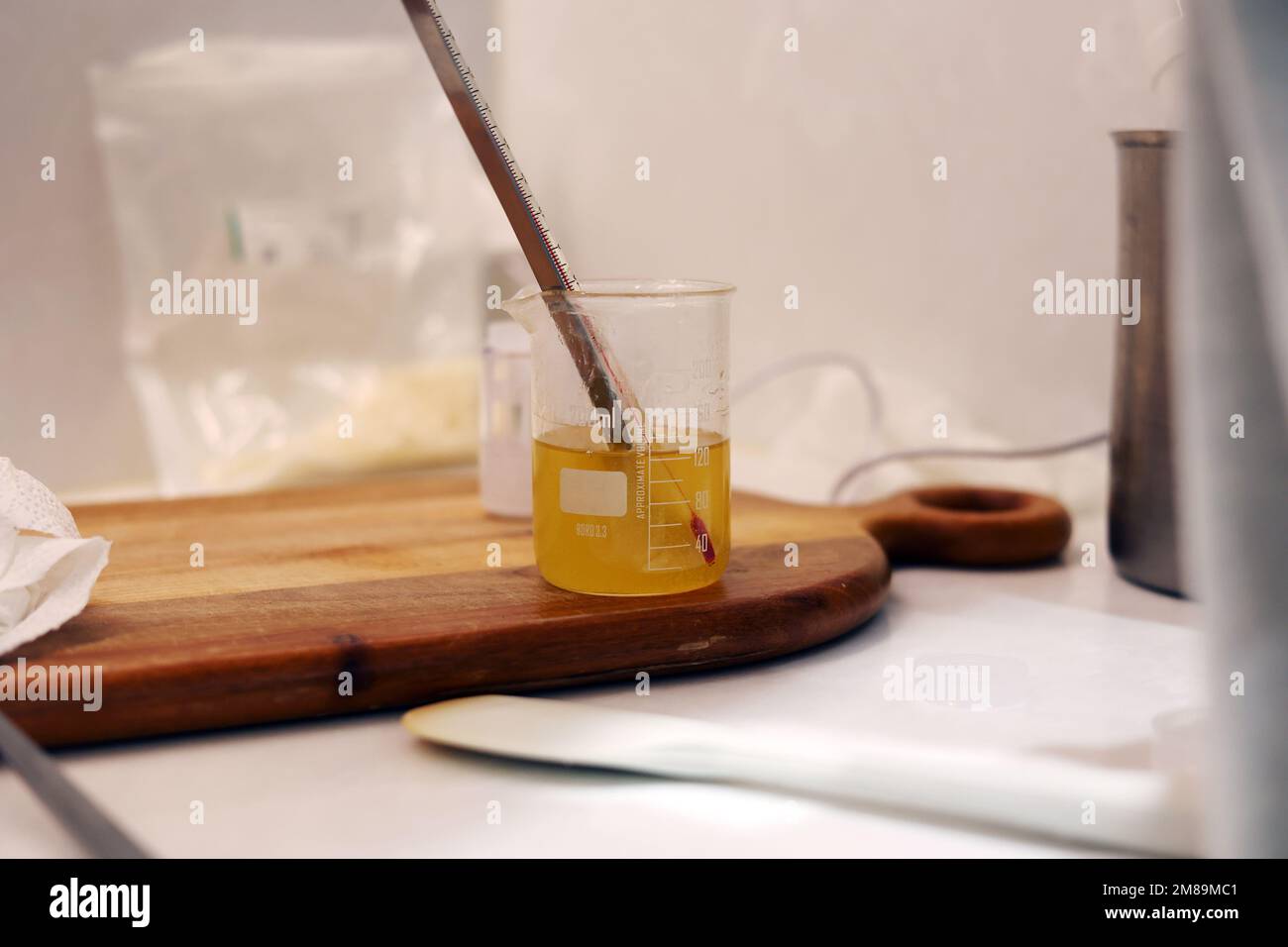 The beaker of jojoba oil with thermometer and spoon in the laboratory ...