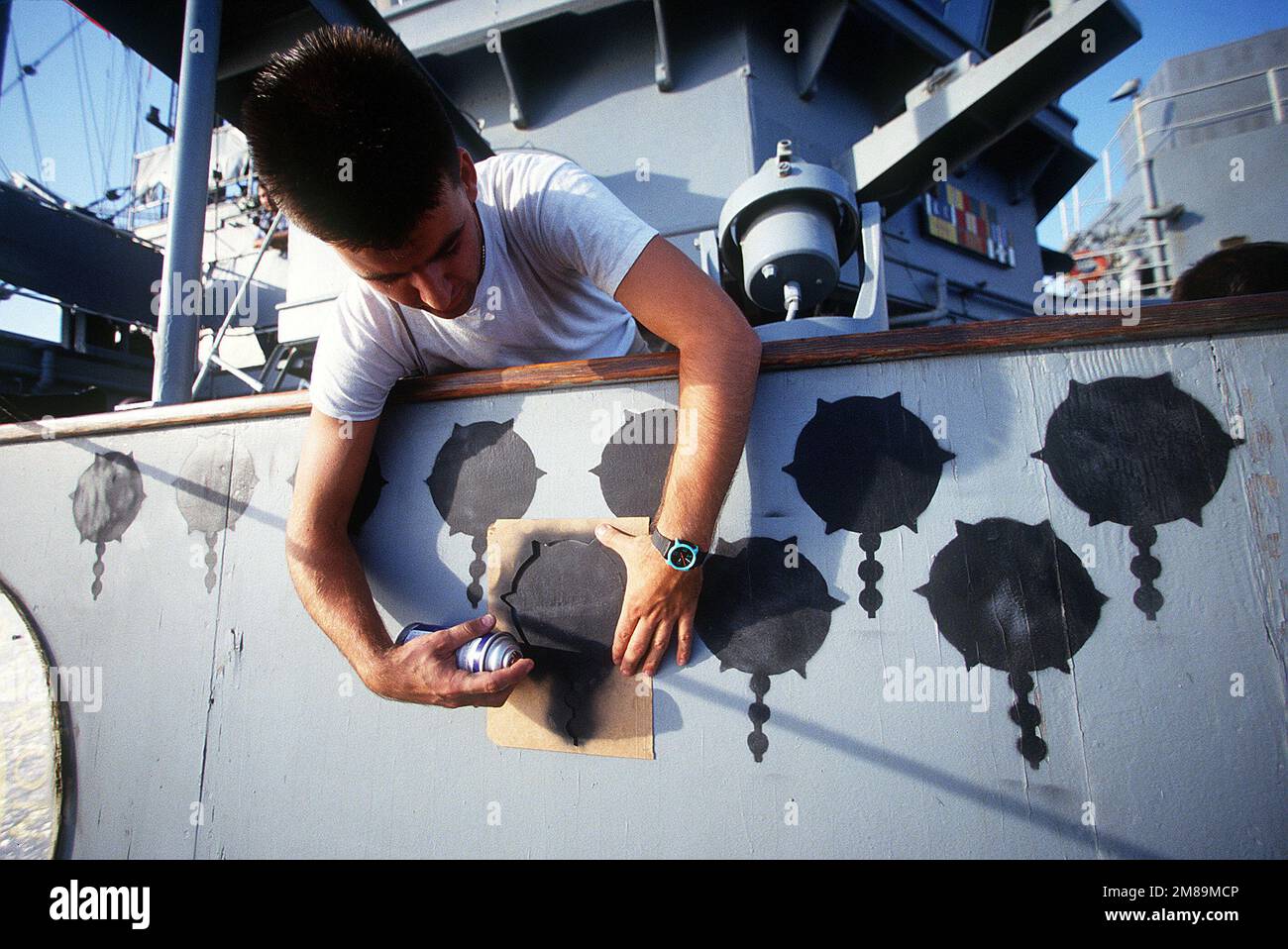 Radioman SEAMAN John M. Joyce spray paints a symbol representing a mine ...