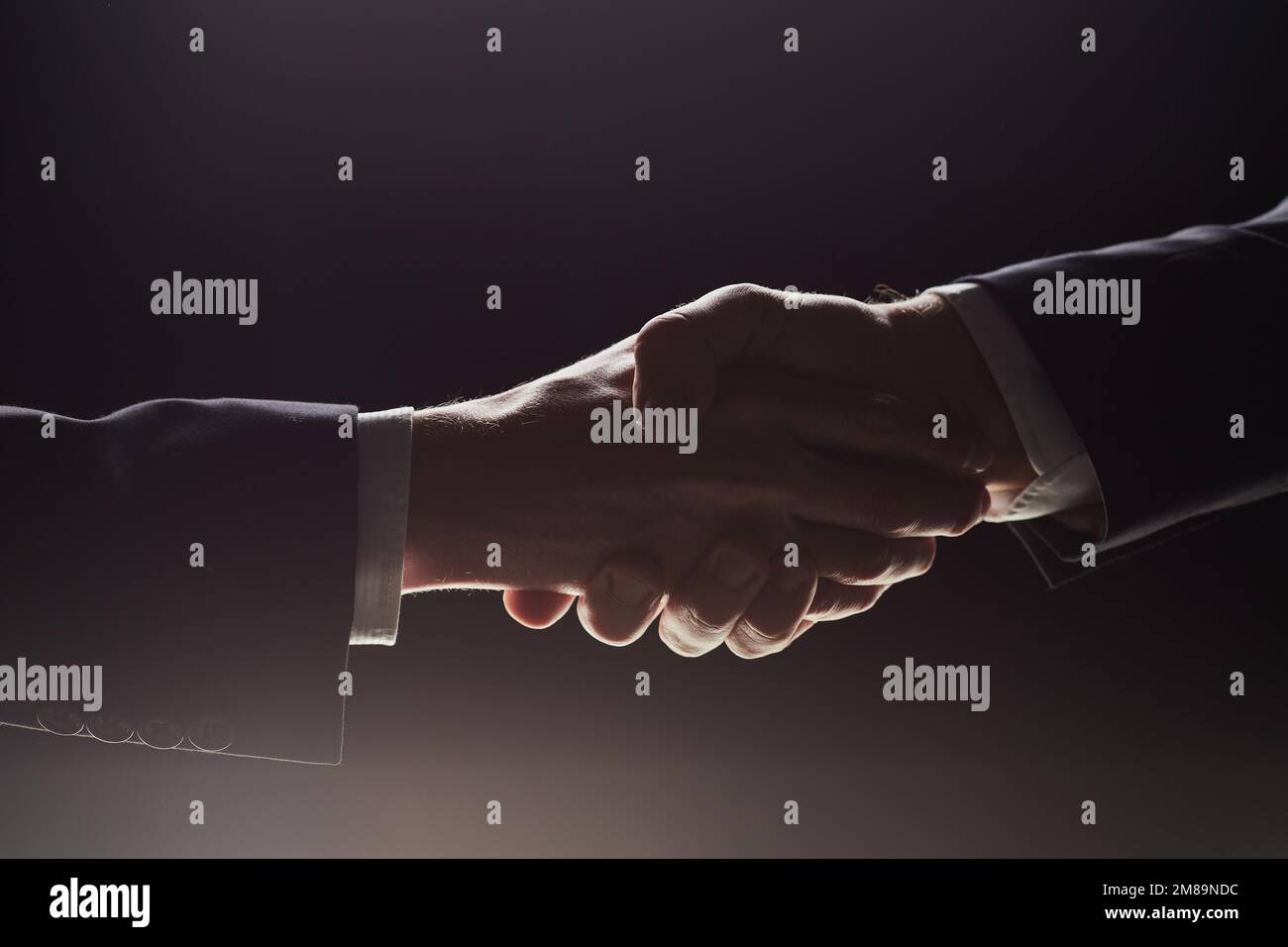 Photo of two men shaking hands on a black background Stock Photo - Alamy