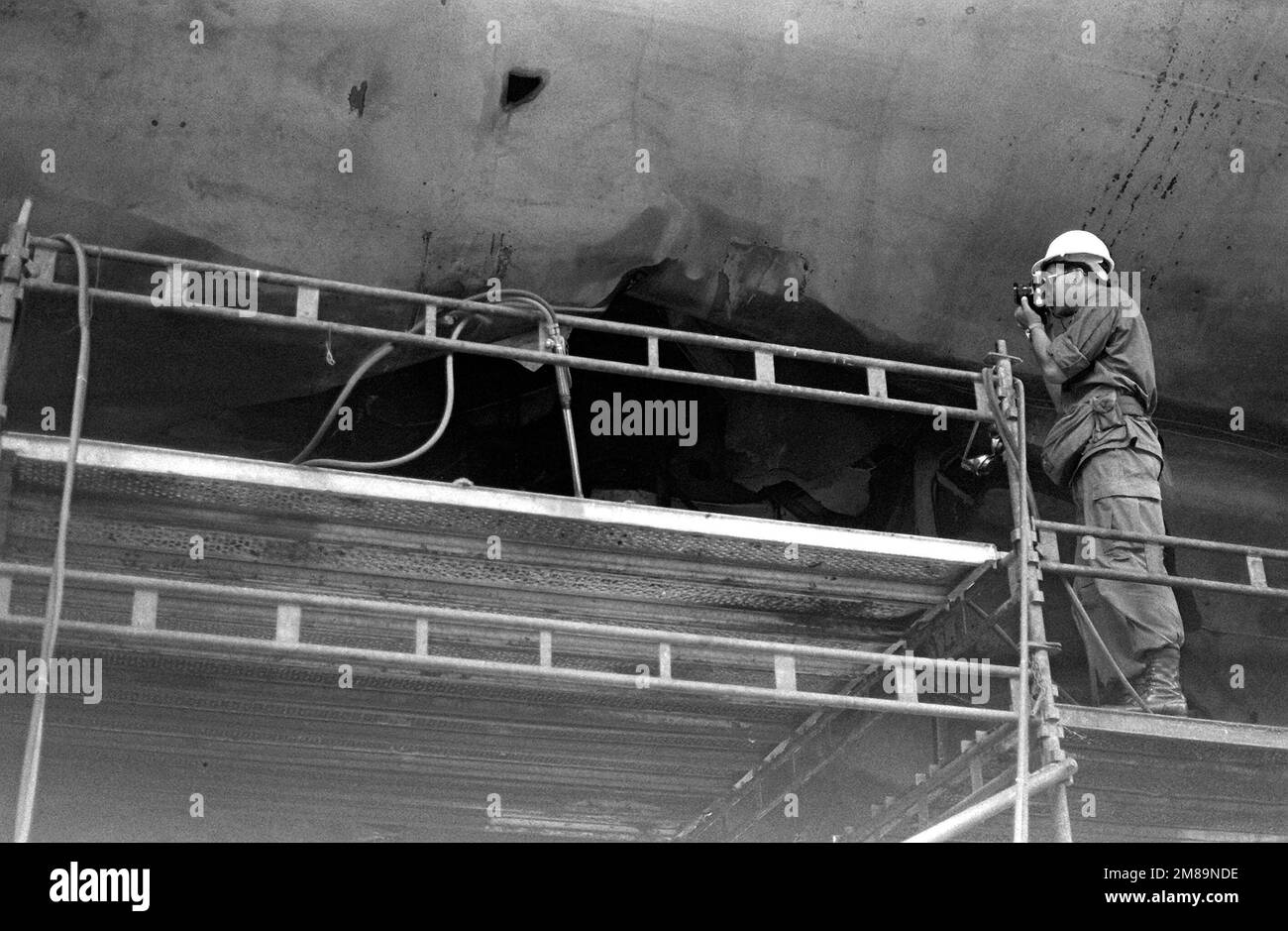 A photographer records the damage to the hull of the guided missile ...