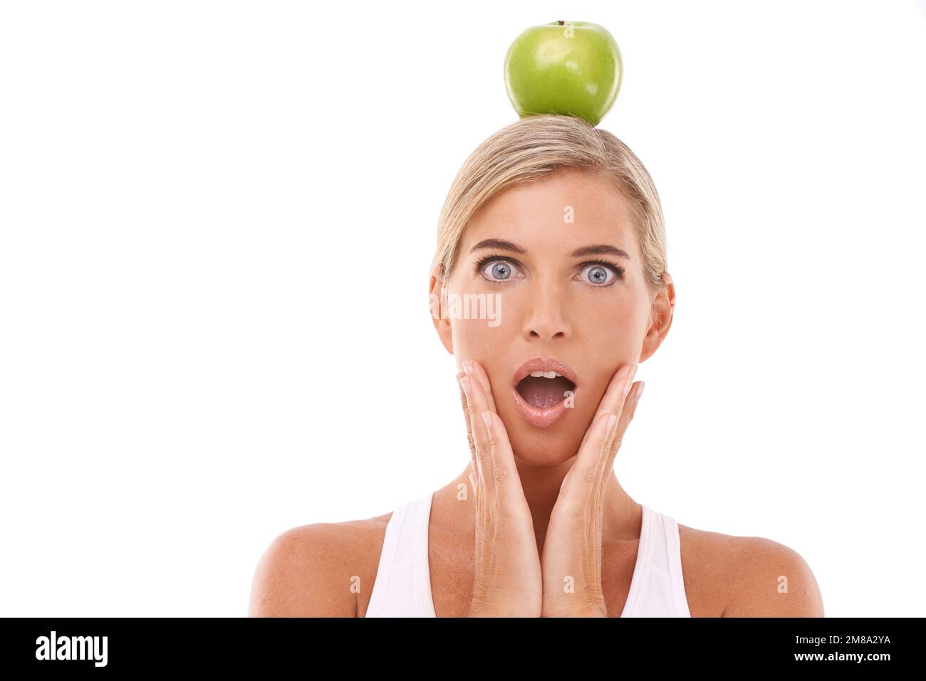 Woman, surprise and apple on head in studio for wellness, nutrition and ...