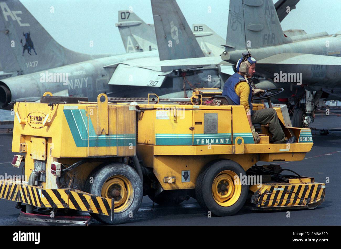 A crewman operates a Tennant Model 550DN self-propelled deck sweeper on ...