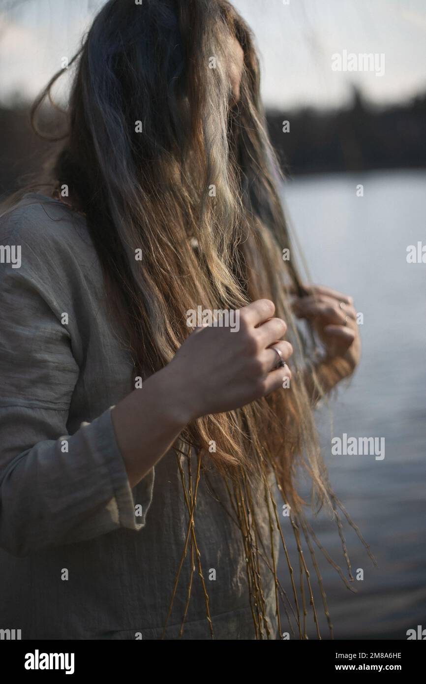Close up woman in linen clothes touching strands of gray brown hair ...