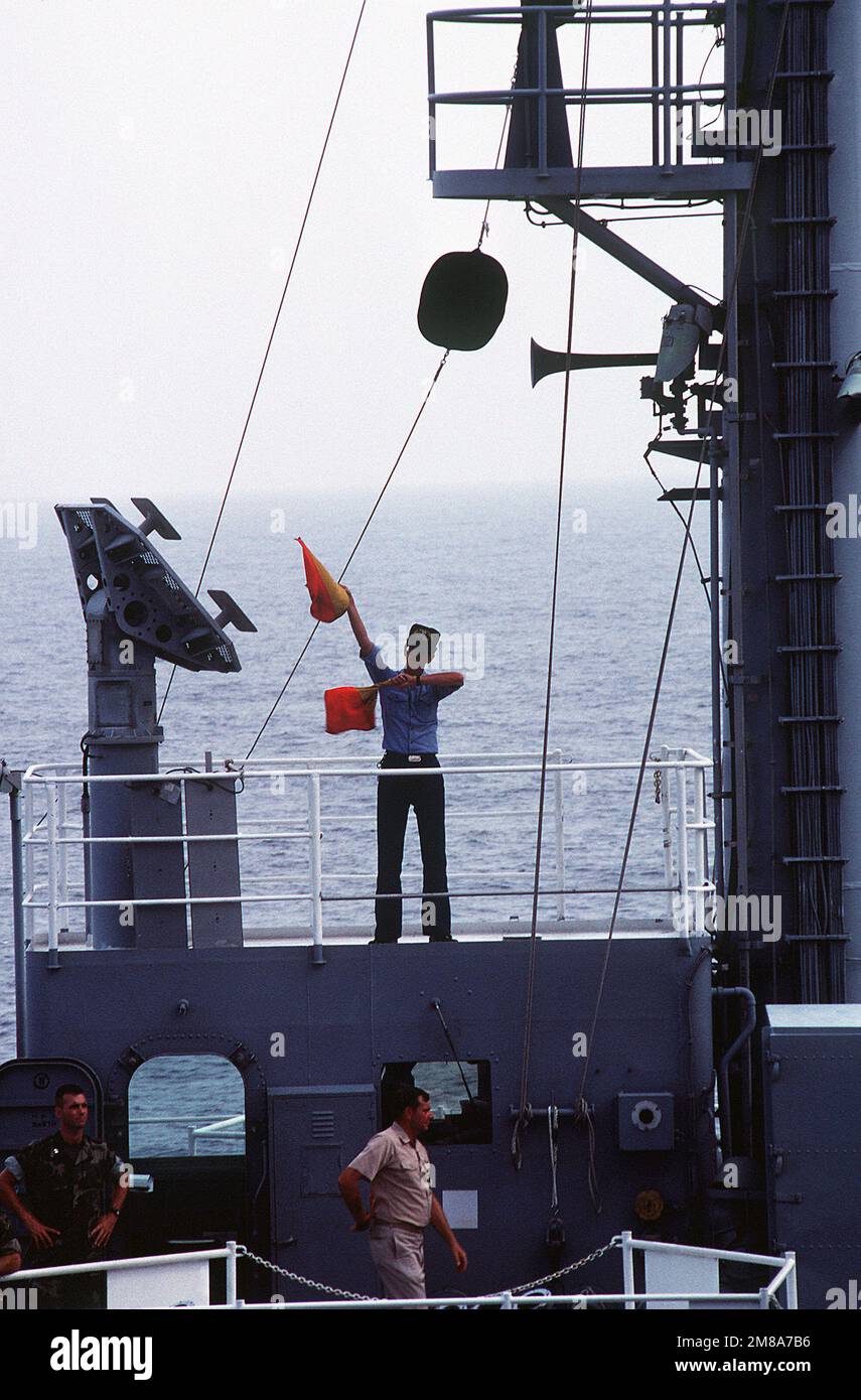 A crewman sends a message with signal flags from the signal bridge of a ...