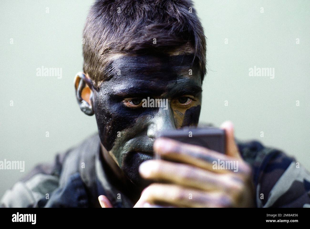 An airman applies camouflage paint to his face before a reconnaissance ...