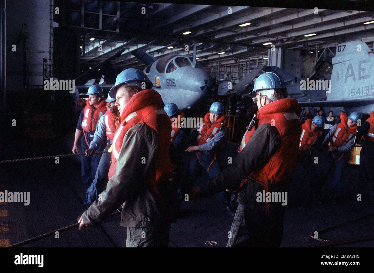 Crewmen hold onto inhaul lines in the hangar bay of the aircraft ...