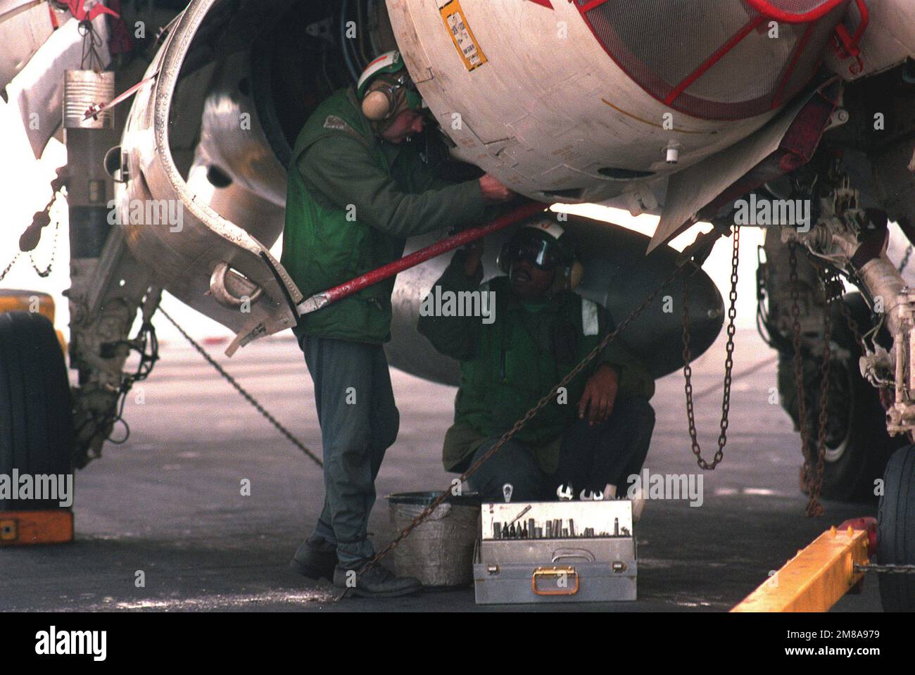 A flight deck crewman services an aircraft engine aboard the aircraft ...