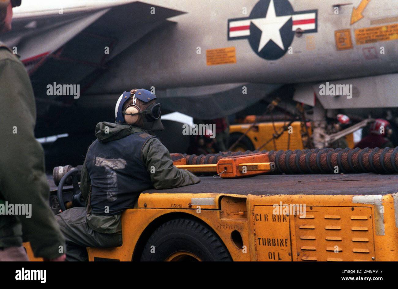 A flight deck crewman positions an MD-3A tow tractor beside an F-14A ...