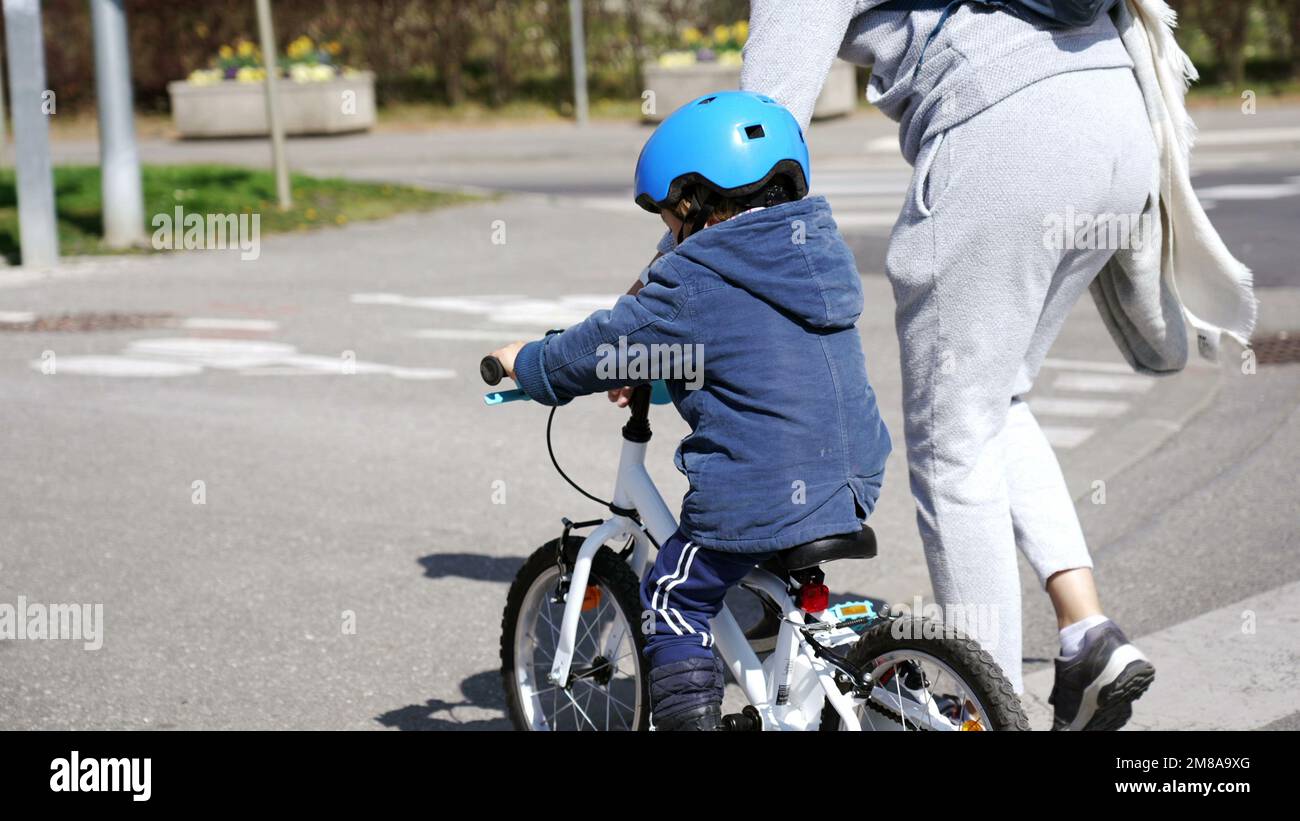 Child cyclist crossing street with mother on zebra lines crosswalk ...