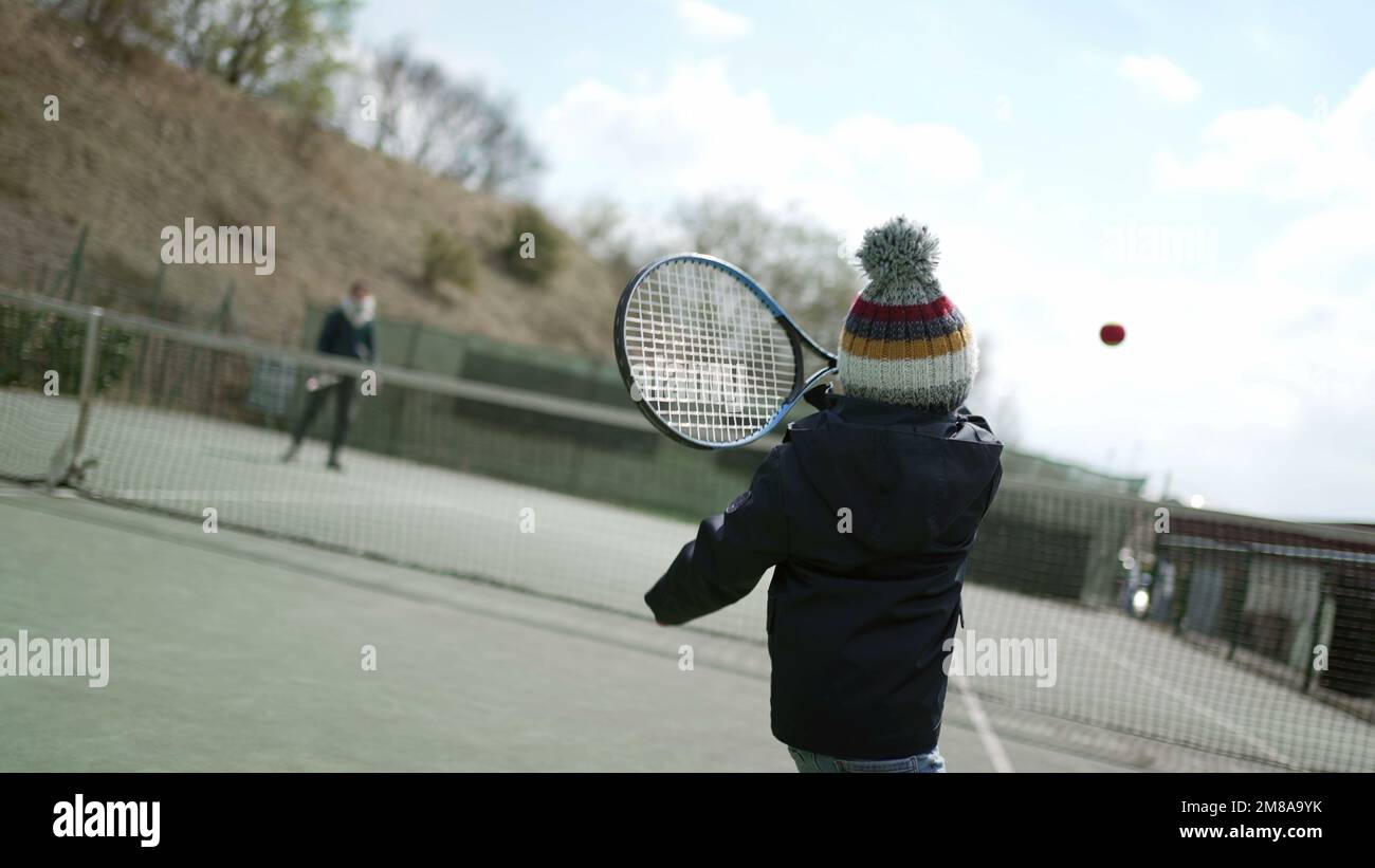 Child hitting ball with tennis racket wearing winter clothes during ...