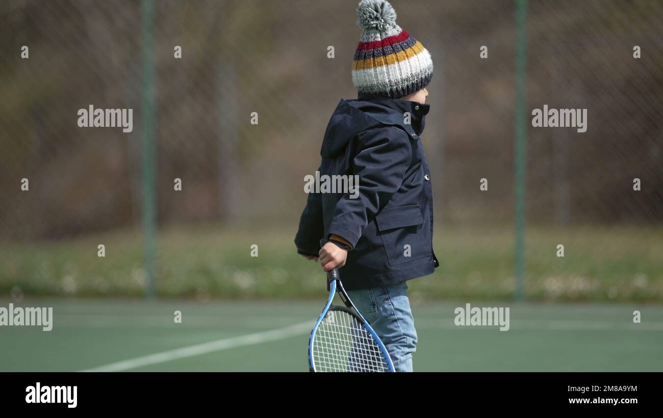 Child hitting ball with tennis racket wearing winter clothes during ...