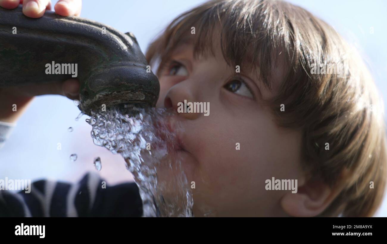 Child drinking water from public faucet outdoors. One little boy ...