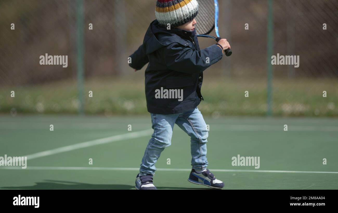 Child hitting ball with tennis racket wearing winter clothes during ...