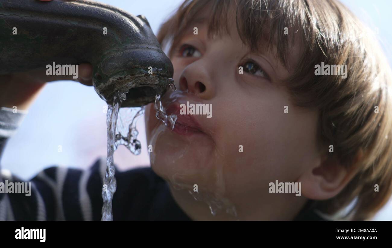 Child drinking water from public faucet outdoors. One little boy ...