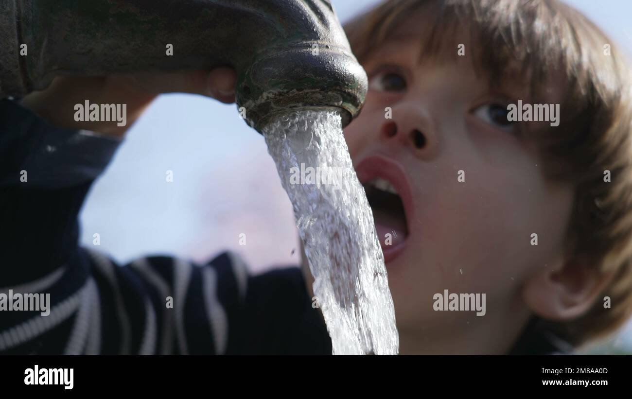 Child drinking water from public faucet outdoors. One little boy ...