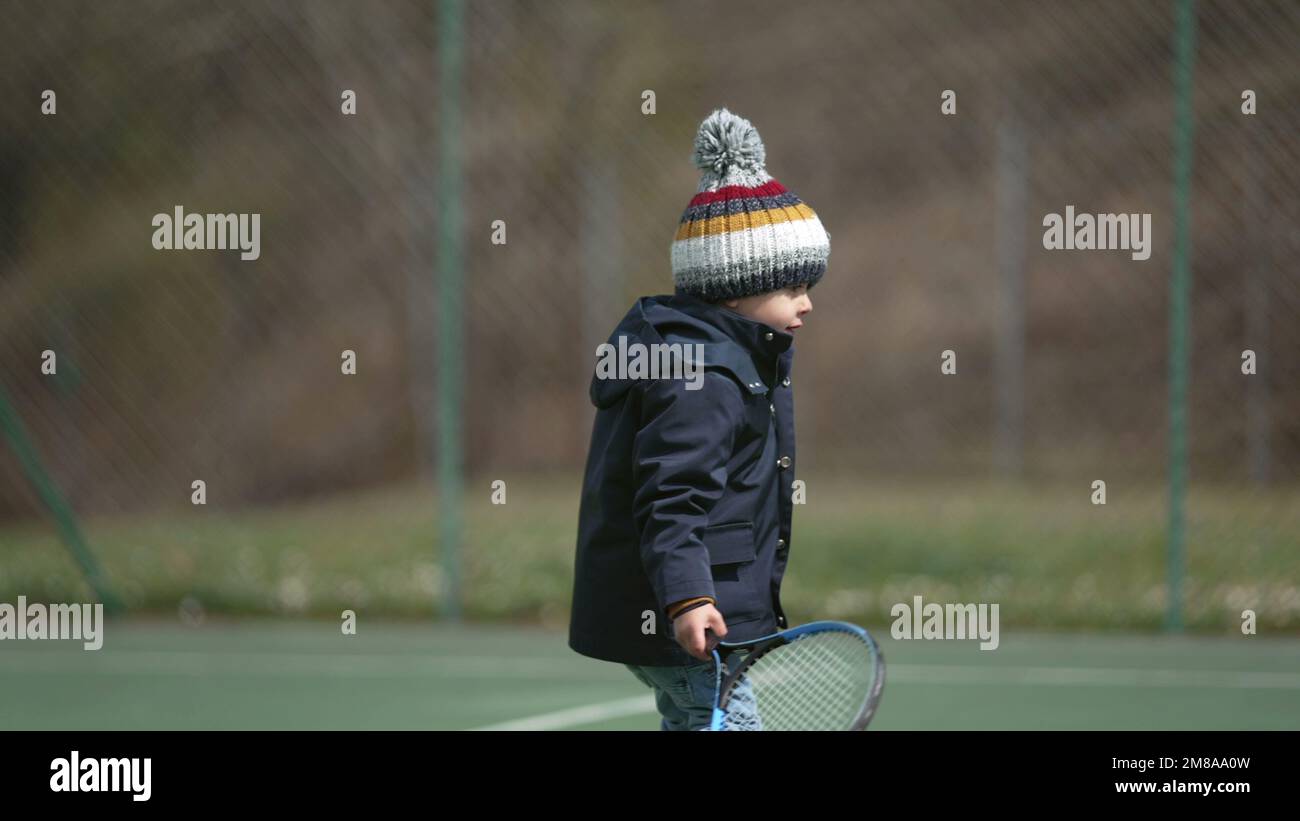 Child hitting ball with tennis racket wearing winter clothes during ...