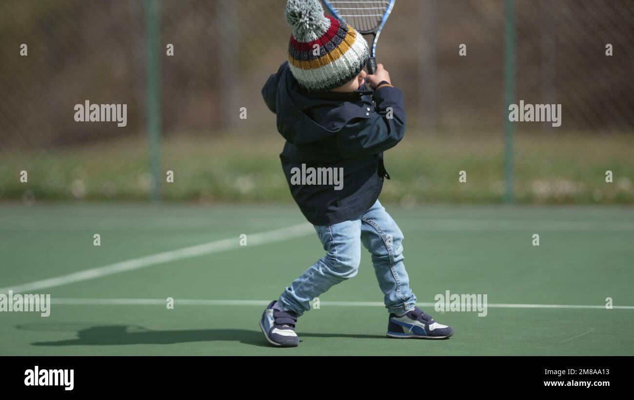 Child hitting ball with tennis racket wearing winter clothes during ...